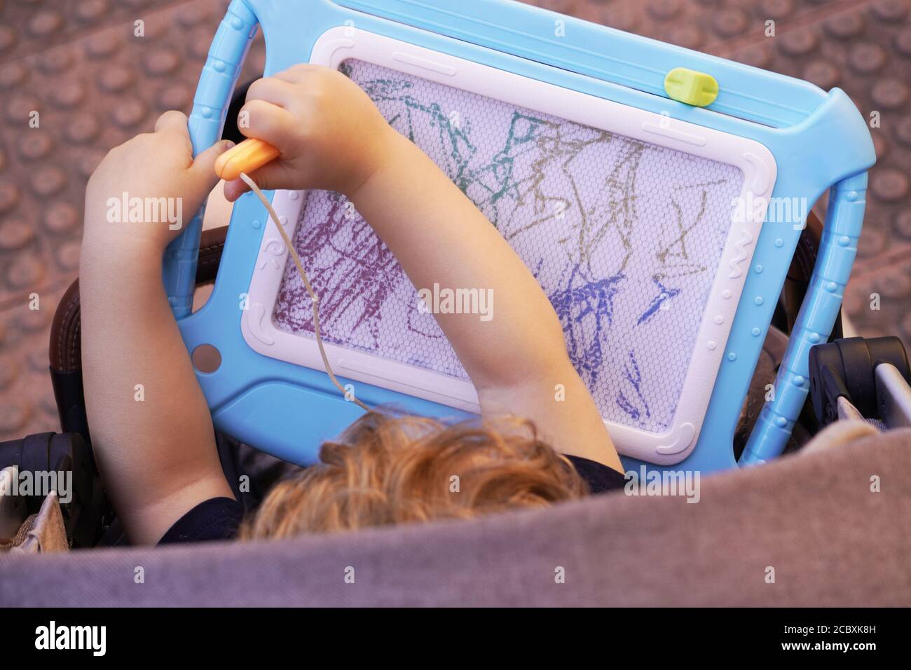 top view of boy sitting in a stroller painting on a blackboard ...