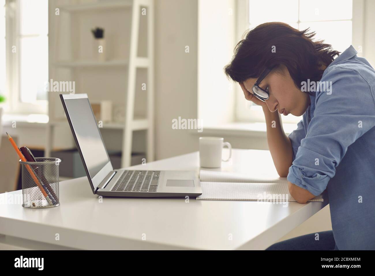 Exhausted young woman working on difficult task in front of laptop at ...