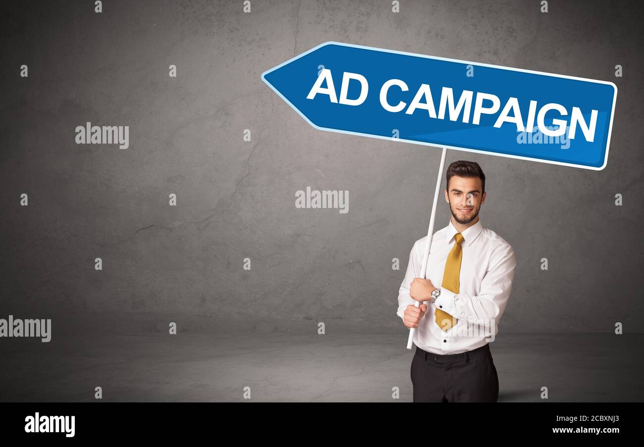 Young business person in casual holding road sign with AD CAMPAIGN ...