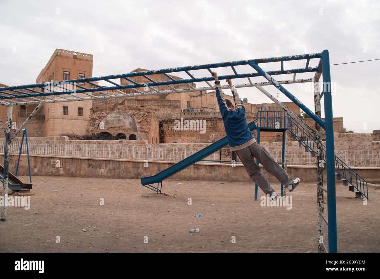 A young Kurdish child playing alone on monkey bars at a playground in ...