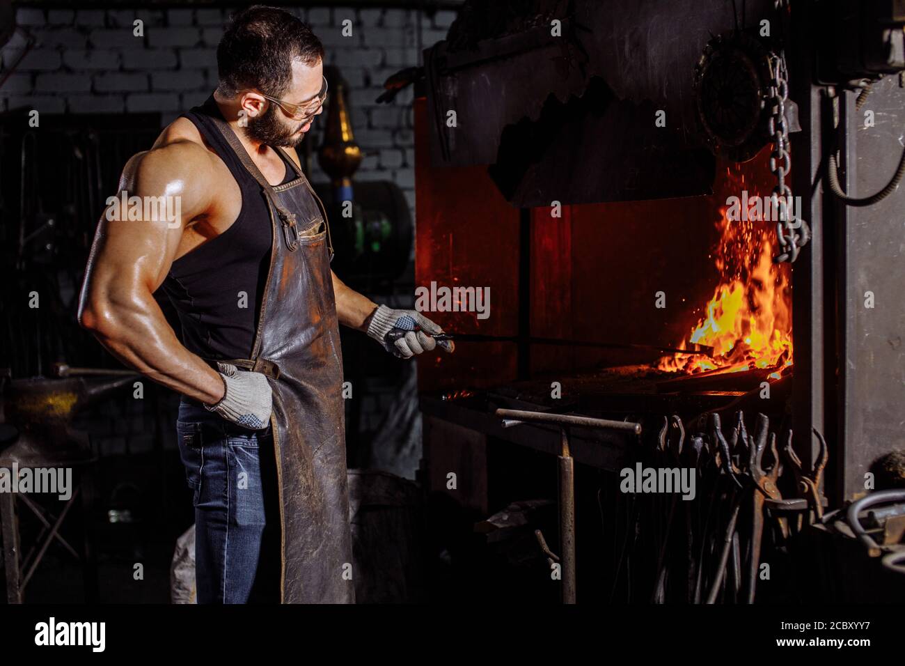 Young caucasian man blacksmith, strong iron worker in workshop, work ...