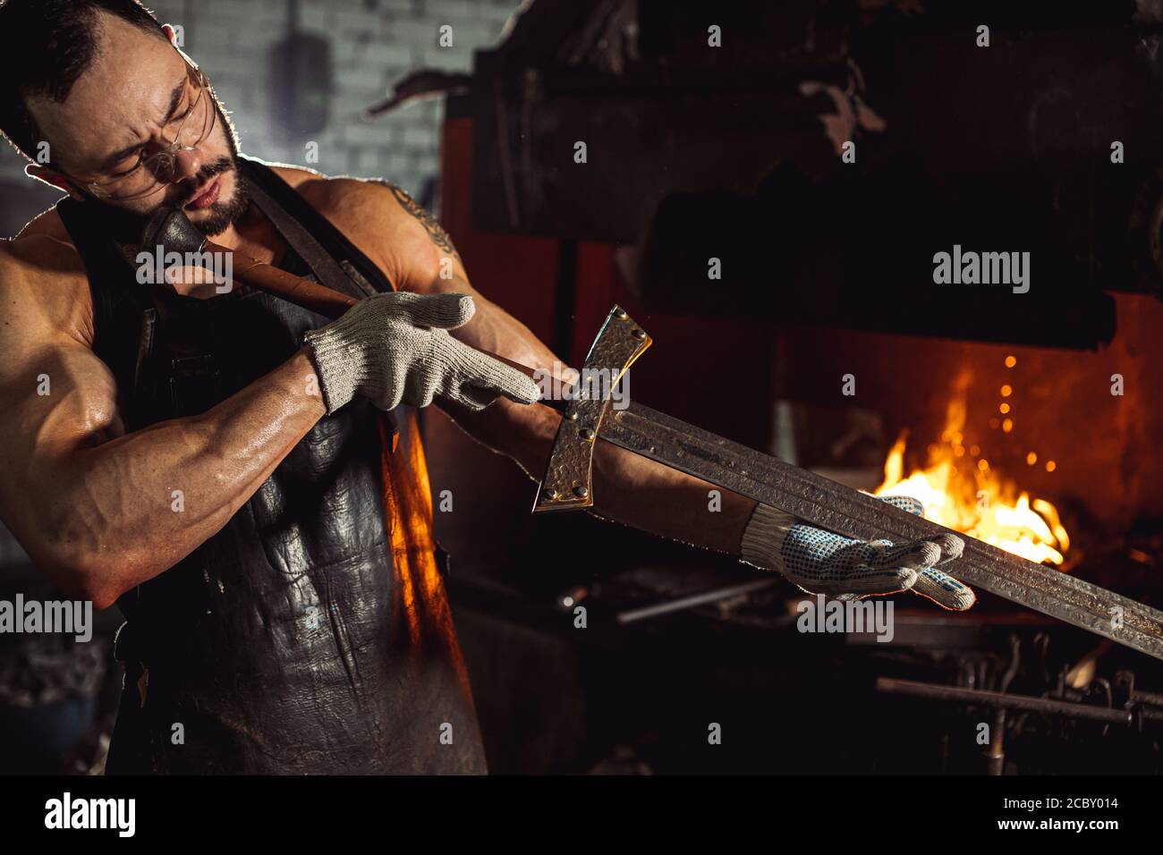 portrait of muscular strong forger studying handmade metal in workshop ...