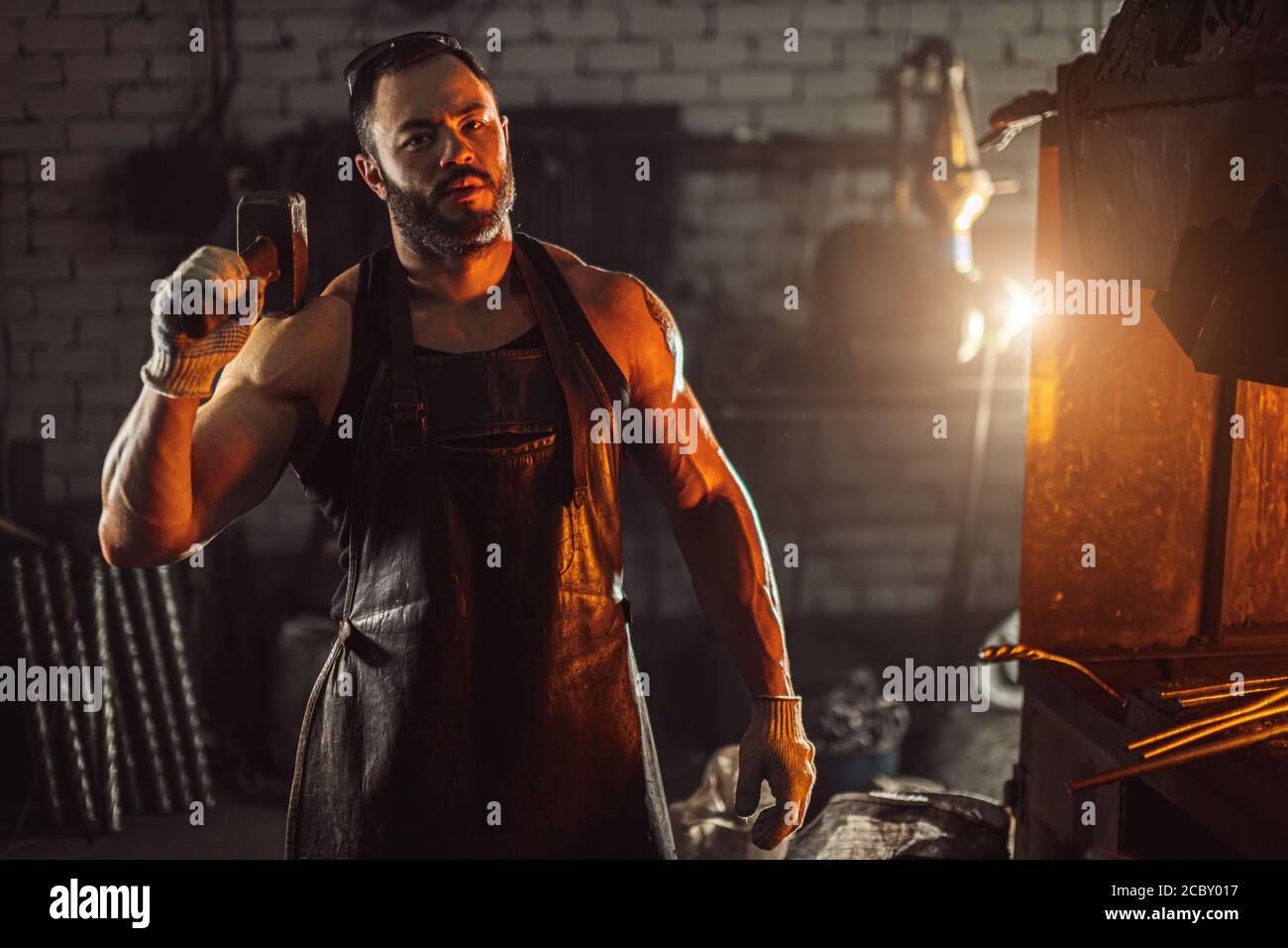 cool caucasian and young blacksmith portrait. forger in work with metal ...