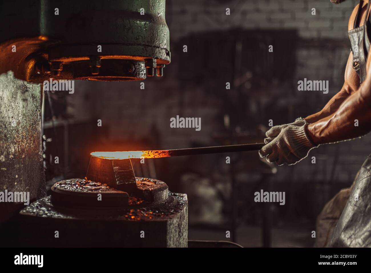 young bearded man in leather uniform heats the metal on fire isolated ...