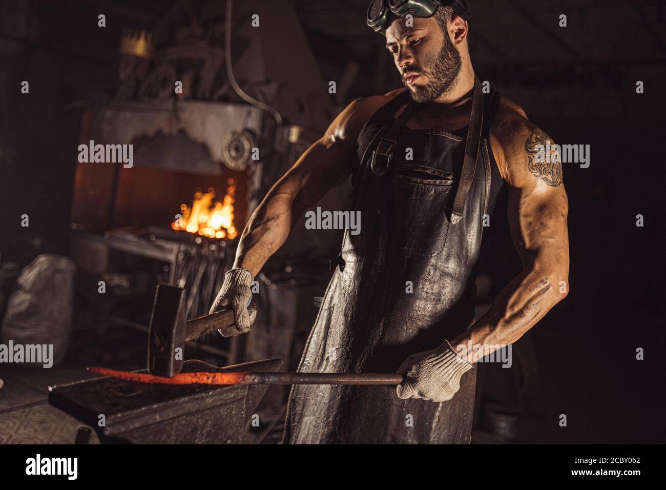 strong muscular brutal confident blacksmith man shaping red hot metal ...