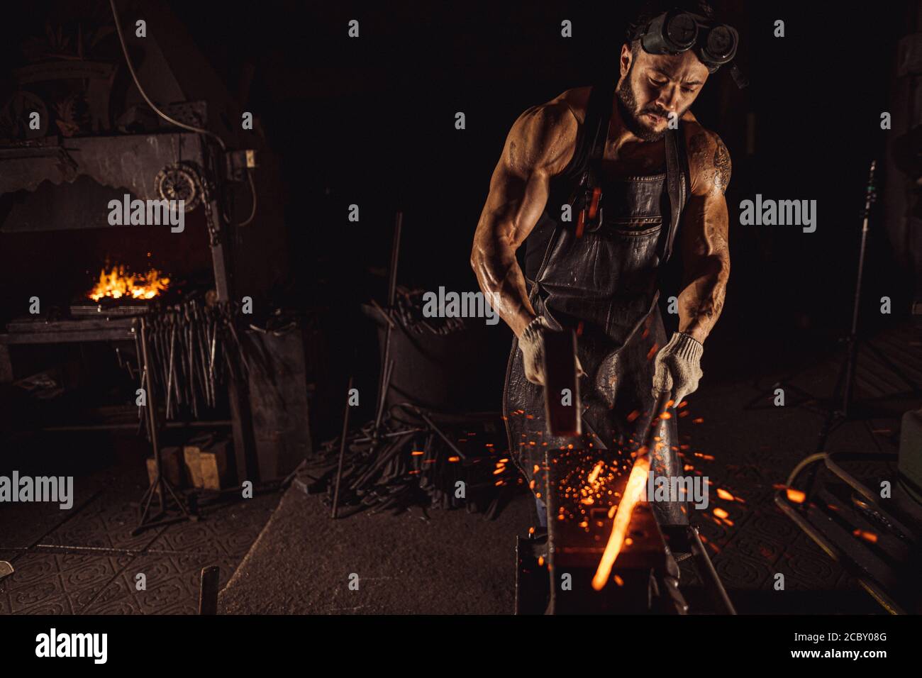 young muscular blacksmith man manually forging the molten metal ...