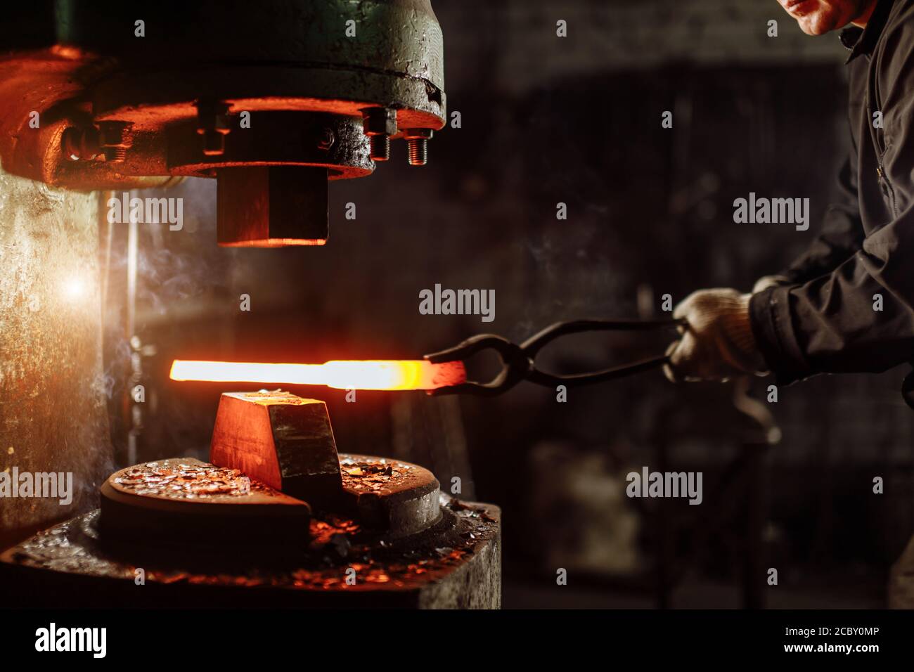 muscular forger man with beard using hydraulic press for steel arms ...