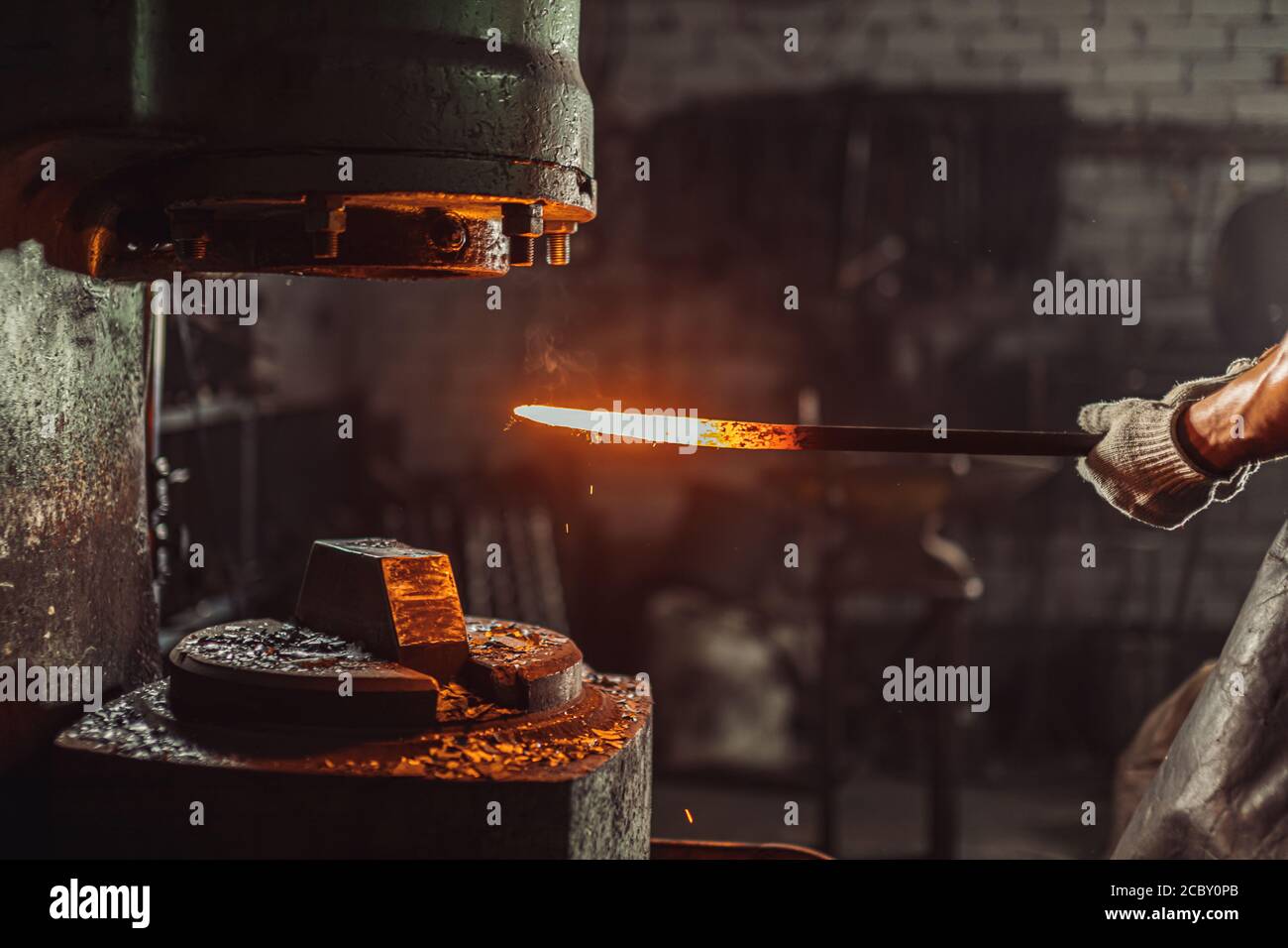 Young forger shaping metal on a jackhammer in the blacksmith workshop ...