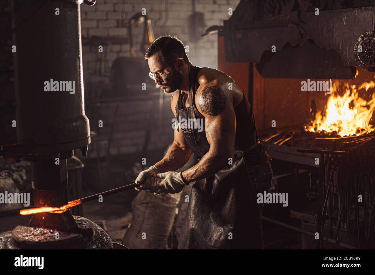 Young forger shaping metal on a jackhammer in the blacksmith workshop ...