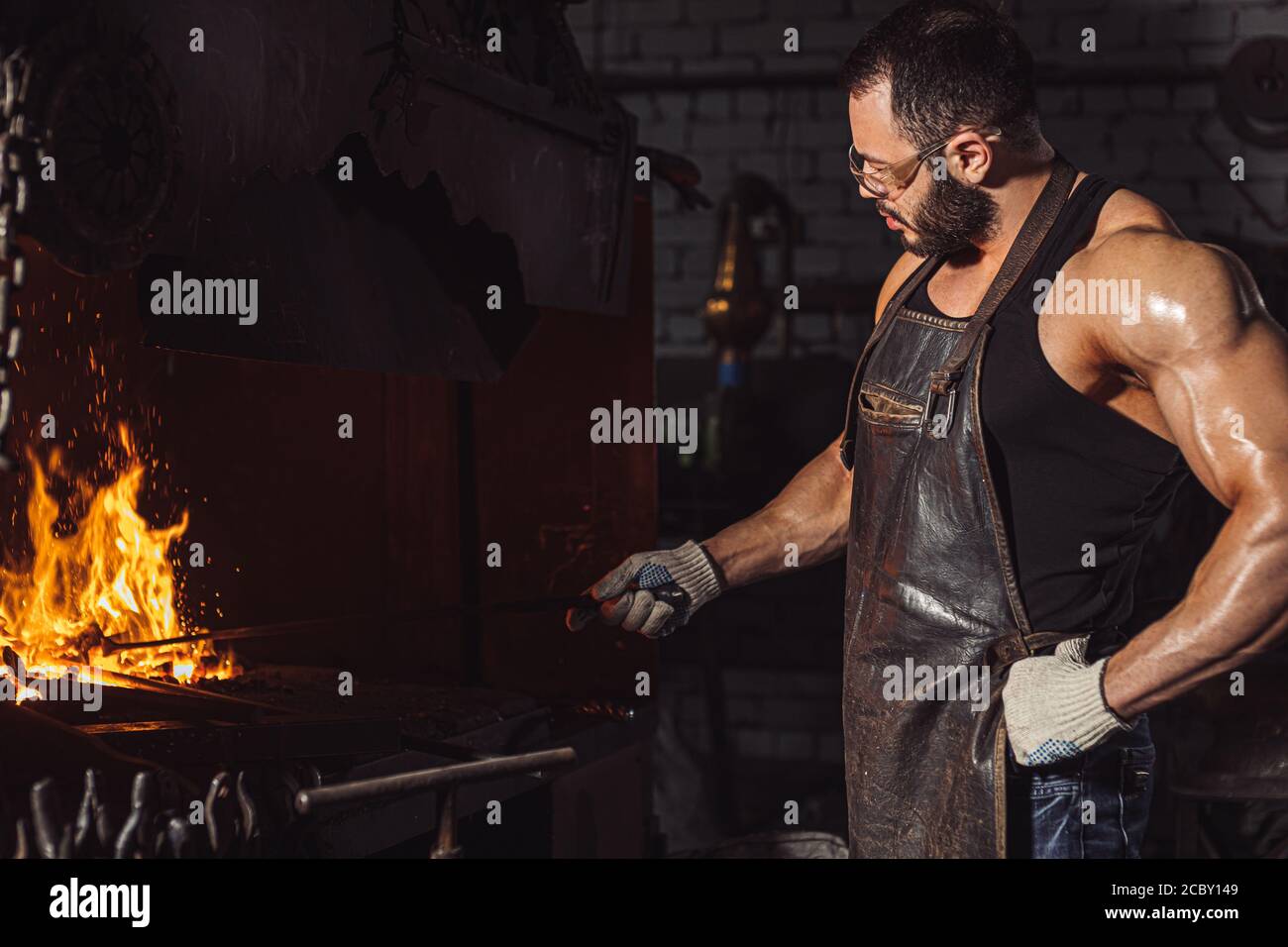 young bearded caucasian man blacksmith heating metal in furnace, have ...
