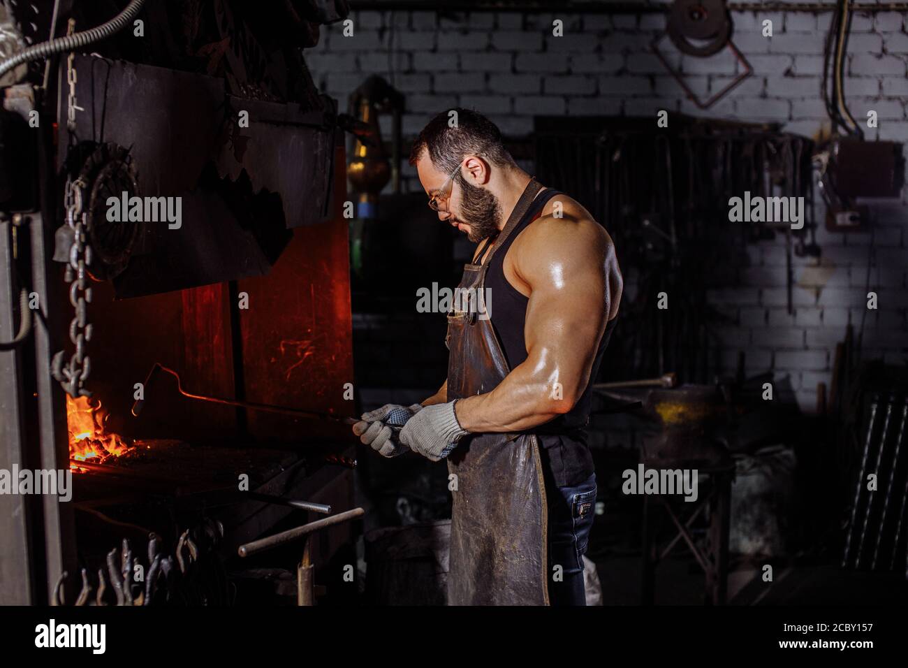 young strong muscular blacksmith wearing black apron and gloves for ...