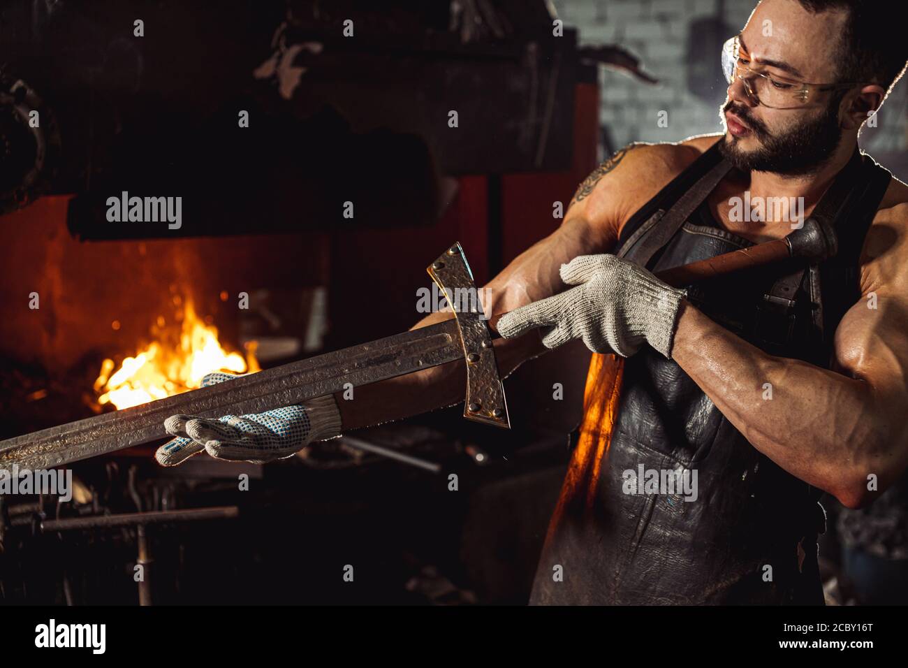 young bearded forger man studying handmade metal in workshop near ...