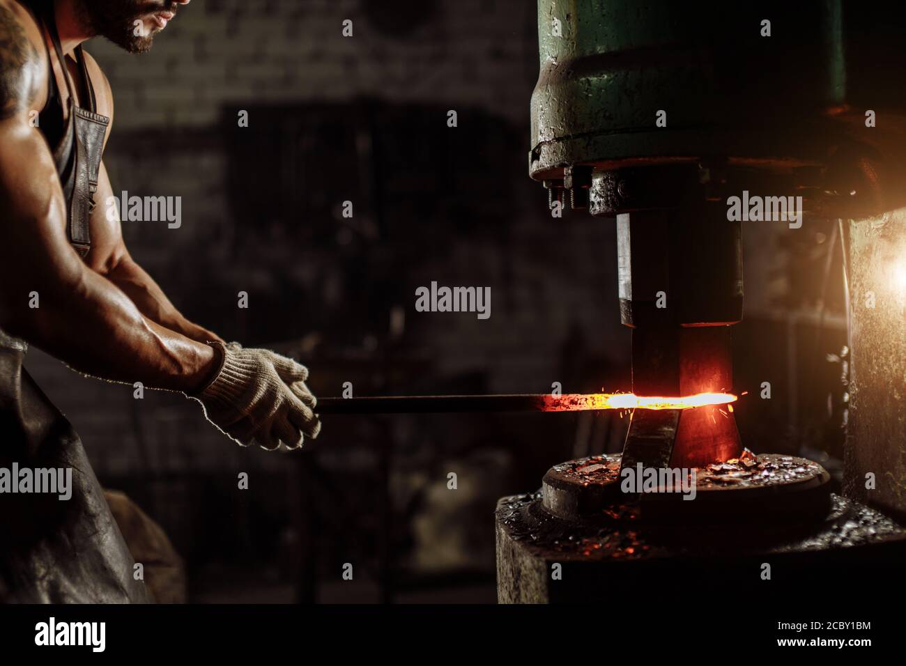 muscular forger man with beard using hydraulic press for steel arms ...
