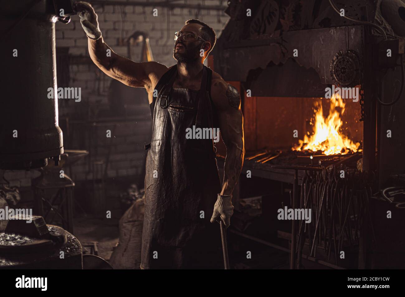 strong muscular blacksmith in good physical form stand with raised hand ...