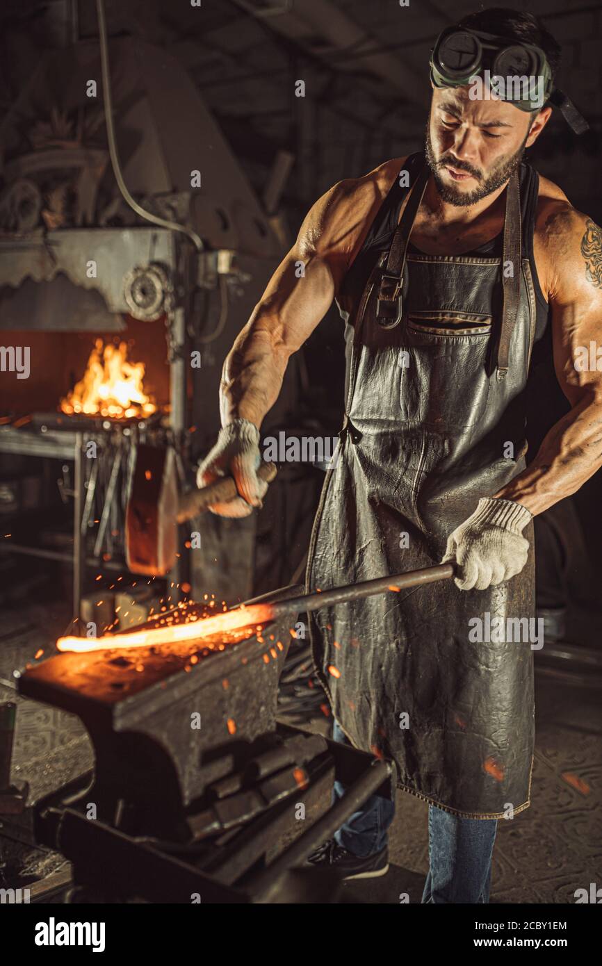 caucasian young man forger having muscular body beat iron with hammer ...