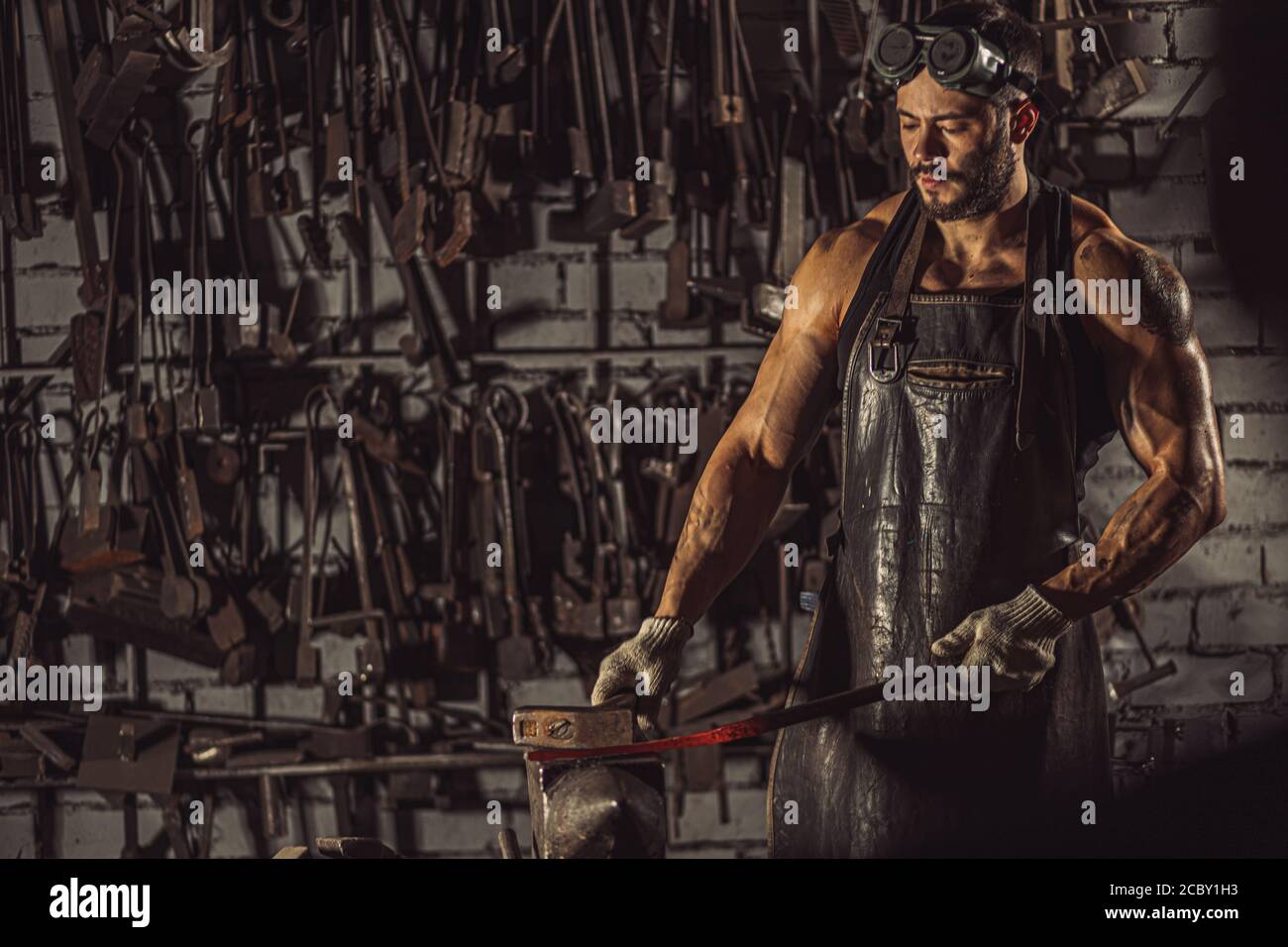 young muscular blacksmith man manually forging the molten metal ...