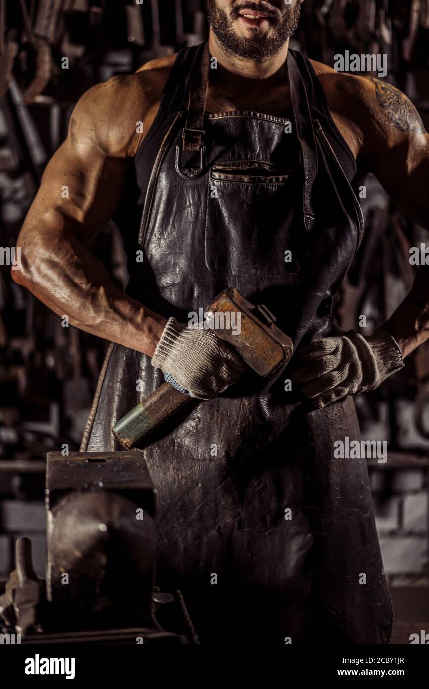 unrecognizable man with muscular body, young blacksmith hold hammer in ...