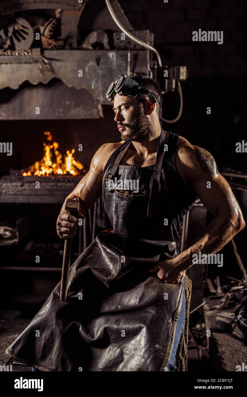 portrait of strong muscular bearded blacksmith or forger sit having ...