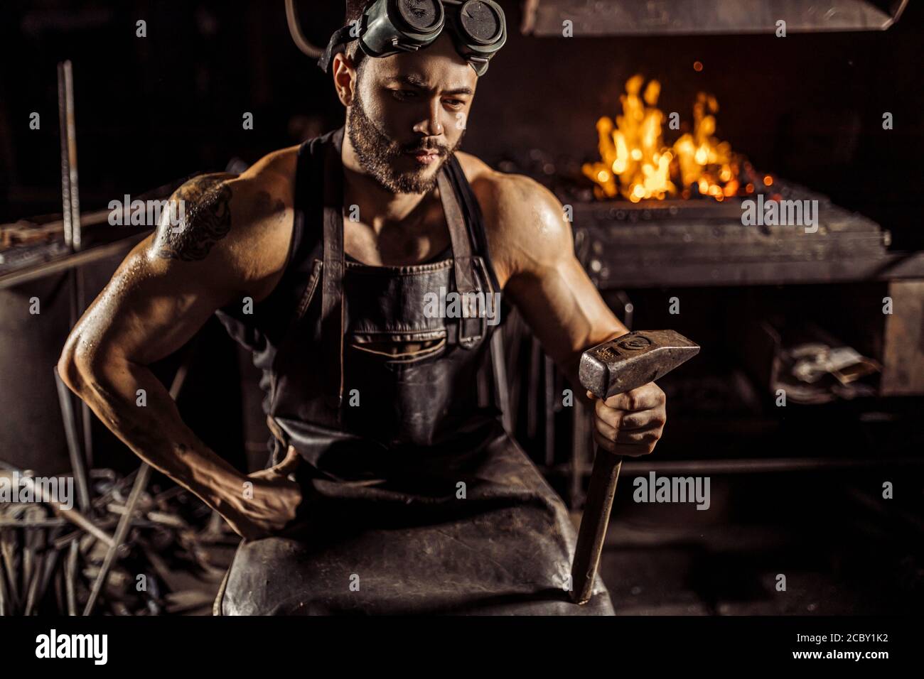 muscular man work at workshop using hammer, wearing leather uniform and ...