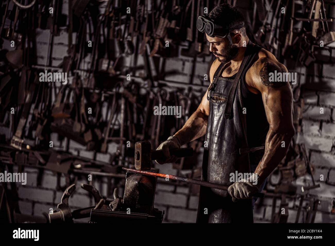 young muscular blacksmith man manually forging the molten metal ...