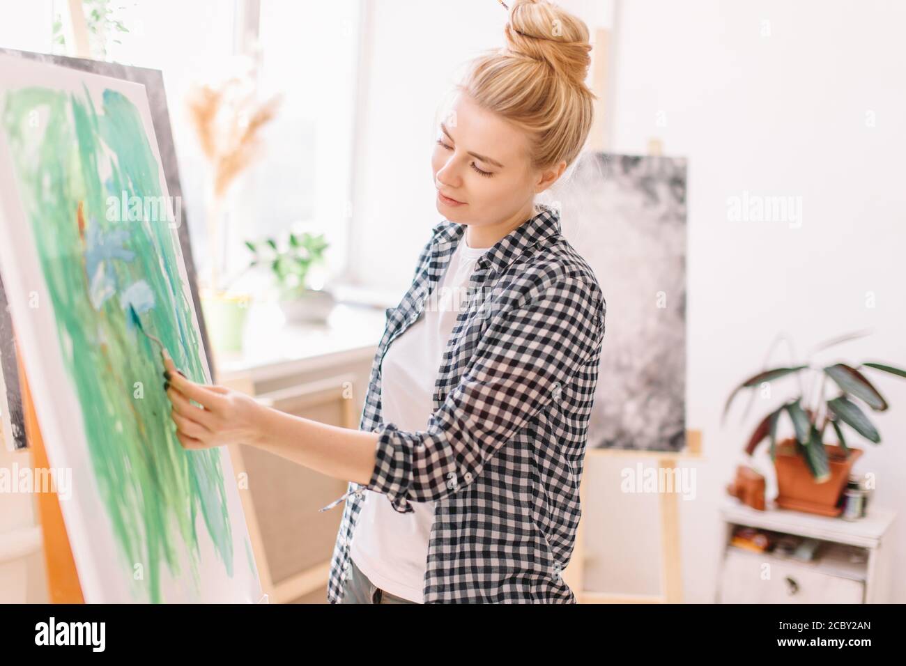 Female awesome artist painting picture, using spatula in workshop ...