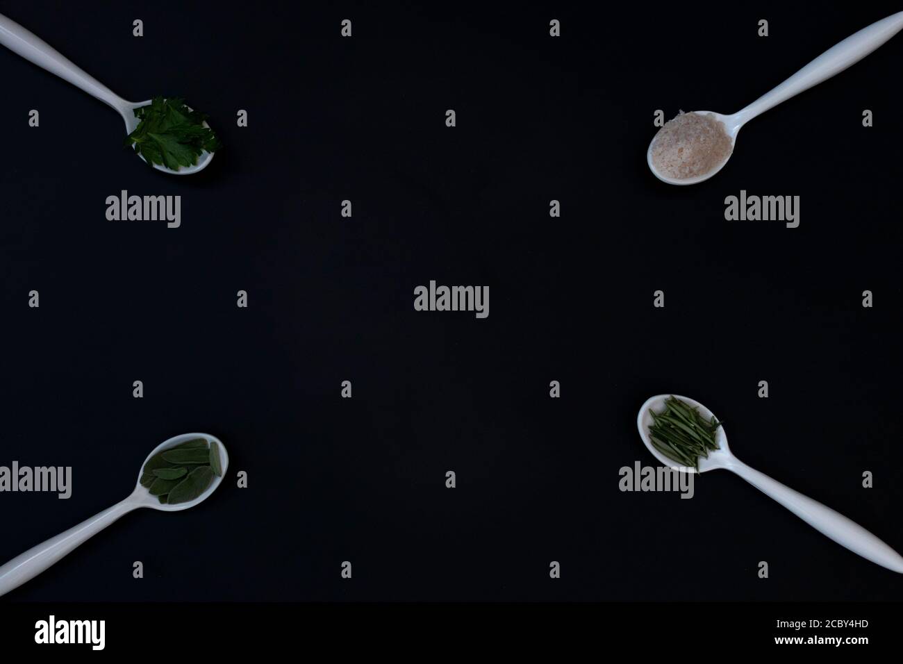 White spoons with herbs spices for cooking. On black background with ...