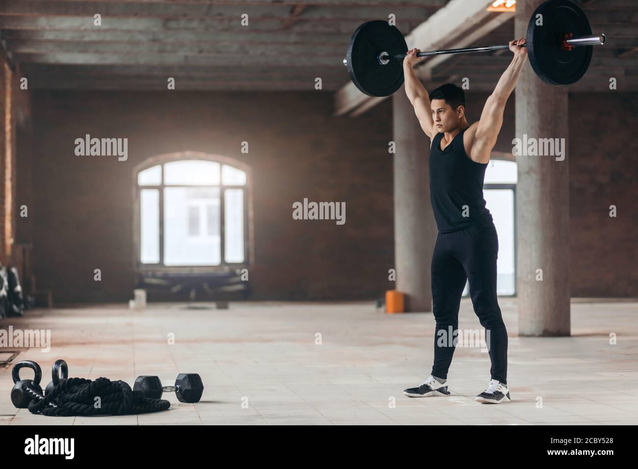 strong man holding heavy weights over his head at gym. full length side ...