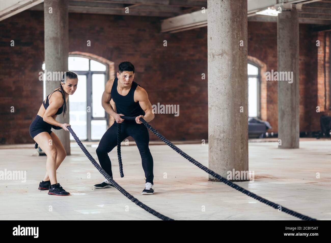 serious guy and girl pulling battle ropes at gym, health and body care ...