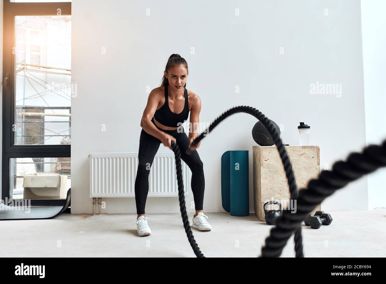 Concentrated Caucasian female doing crossfit exercises using rope in ...