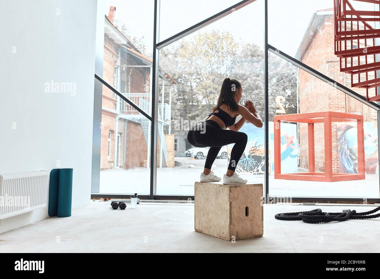 Rear view on Beautiful sporty woman in sportswear jumping on wooden box ...