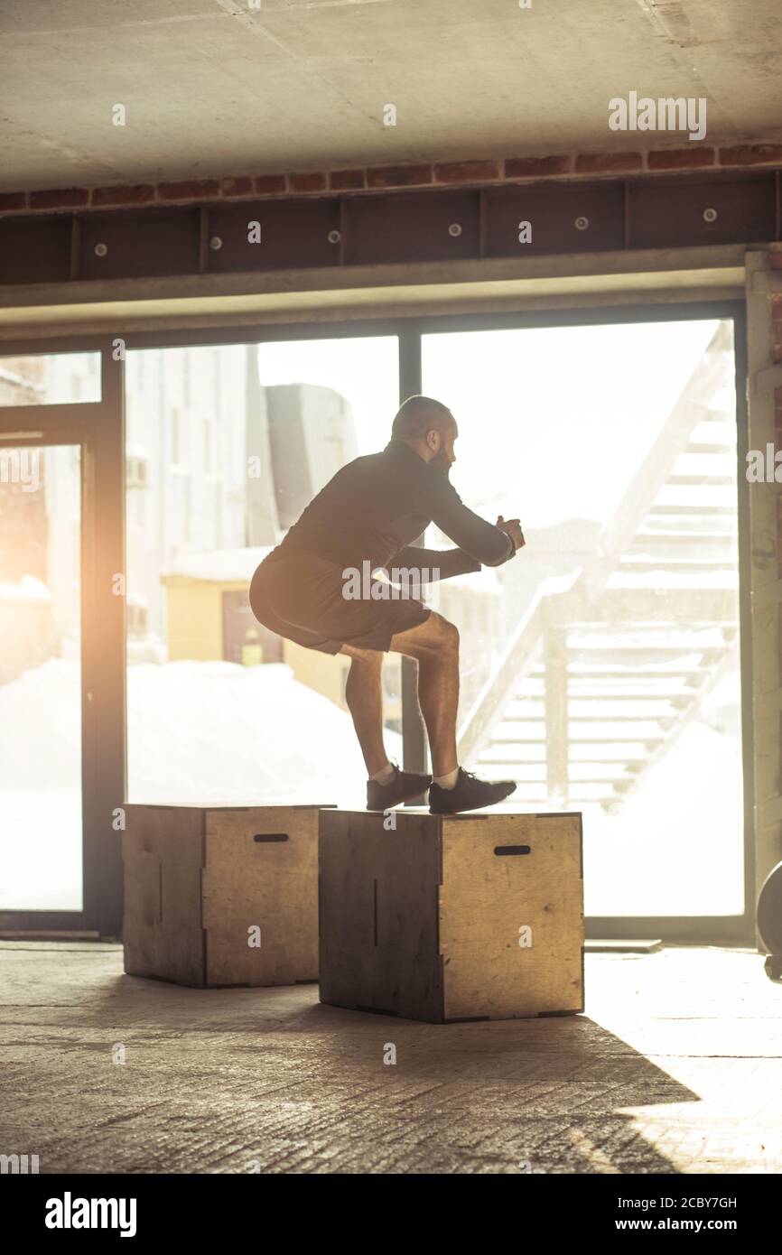 Caucasian determined sportsman performing plyometric box jumps indoor ...