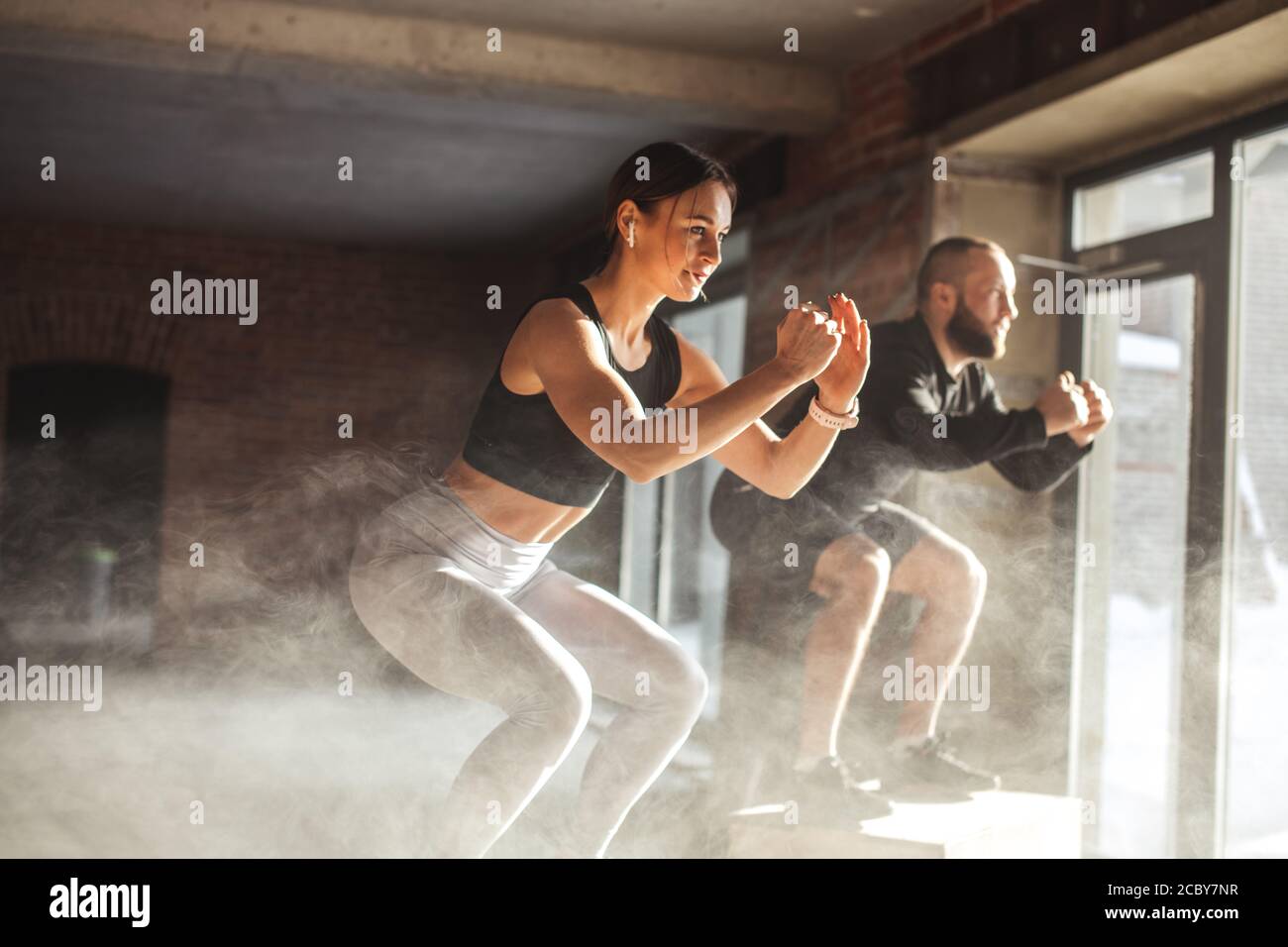 Fit caucasian couple doing squats on boxes in a crossfit style gym ...