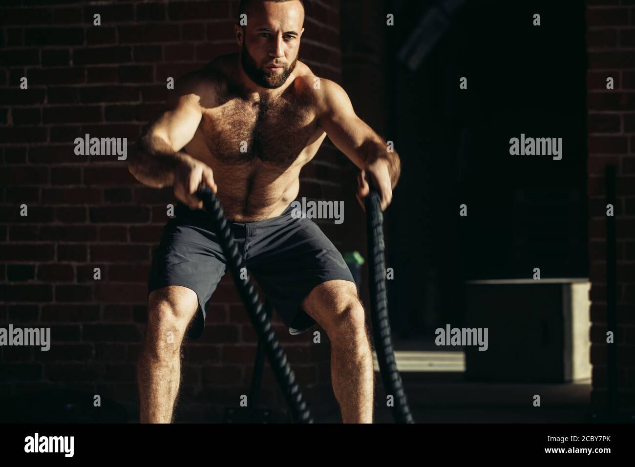 Athletic young man with battle rope doing exercise in functional ...