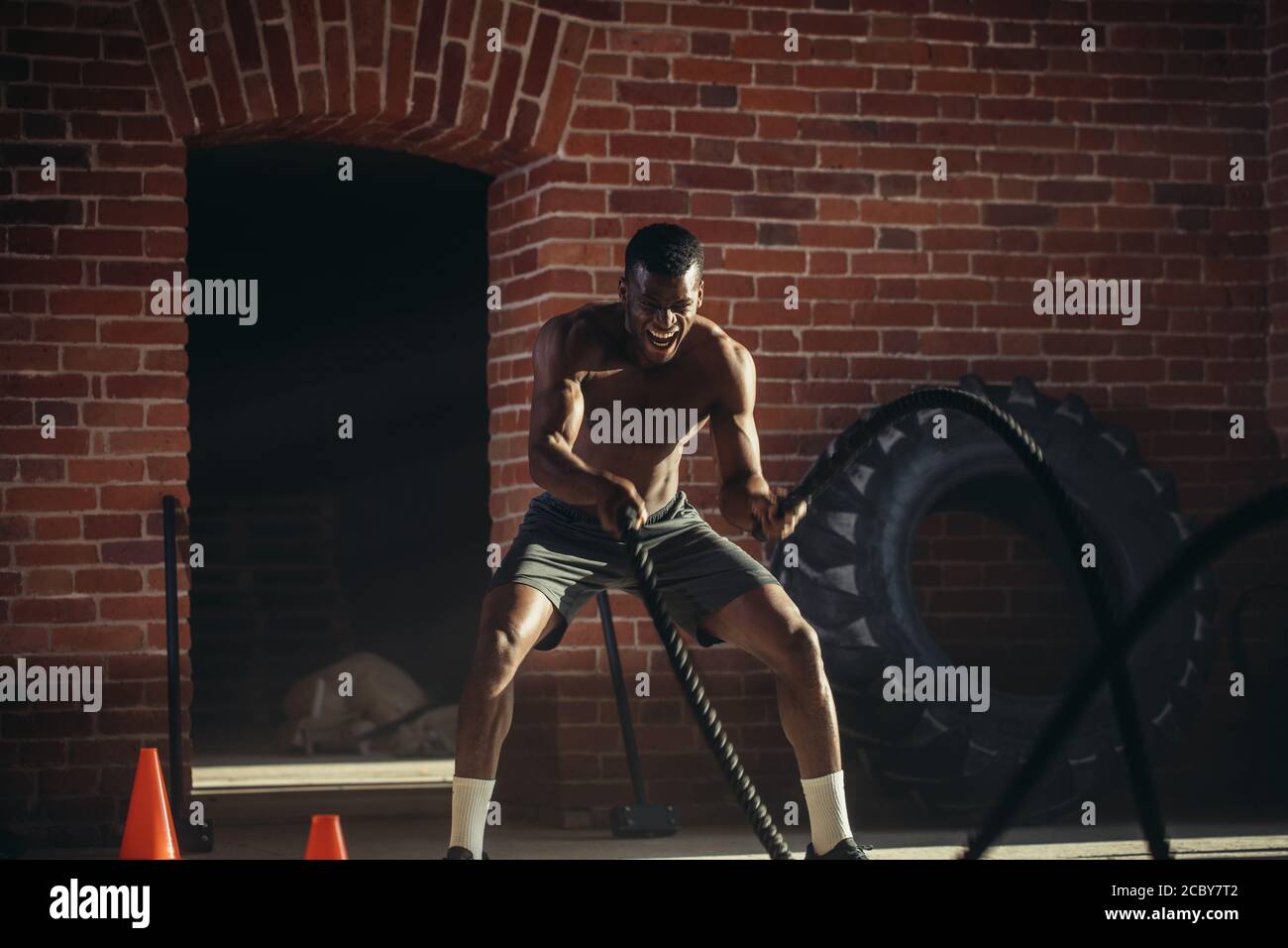 Afro american bodybuilder with battle rope in cross-fit training centre ...