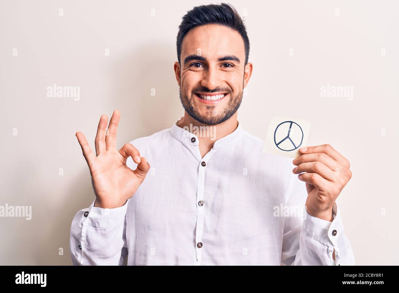 Young handsome man with beard holding reminder with peace symbol over ...