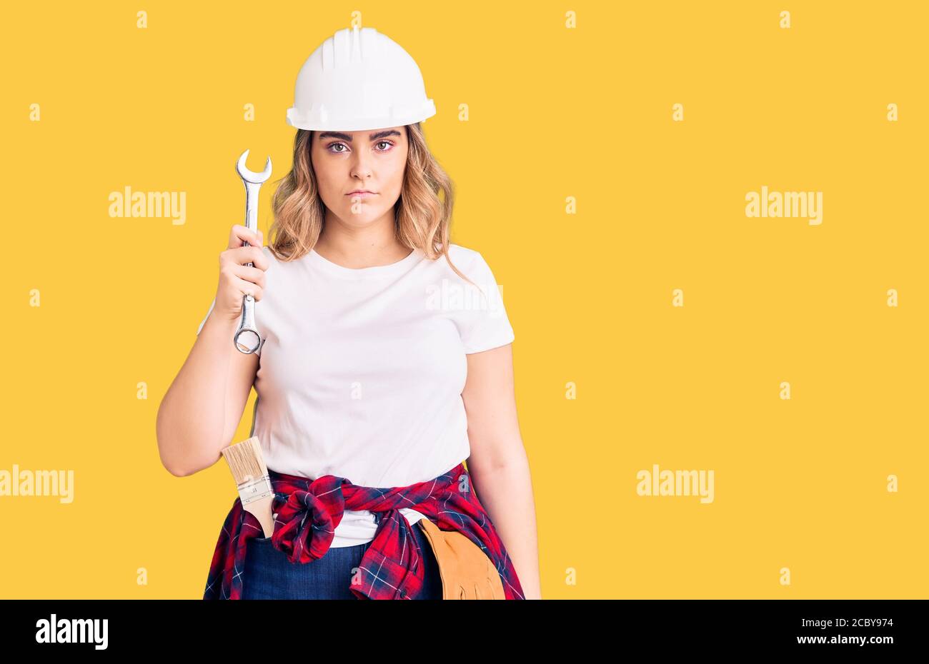 Young caucasian woman wearing hardhat holding wrench thinking attitude ...