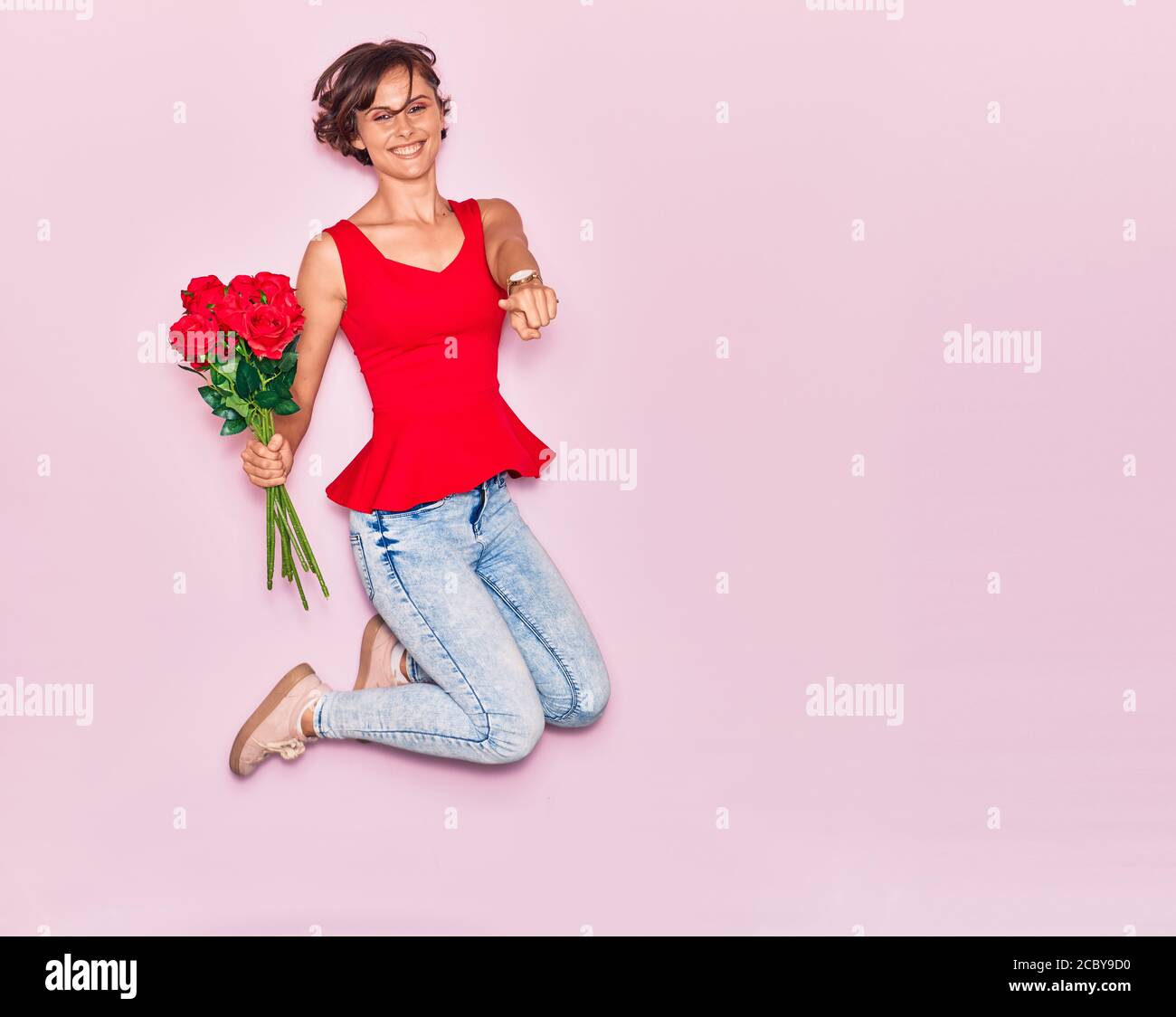 Young beautiful woman holding bouquet of roses smiling happy. Jumping ...