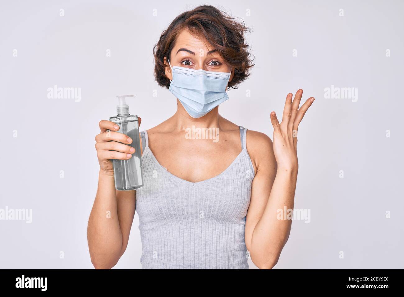 Young hispanic woman wearing medical mask holding hand sanitizer gel ...