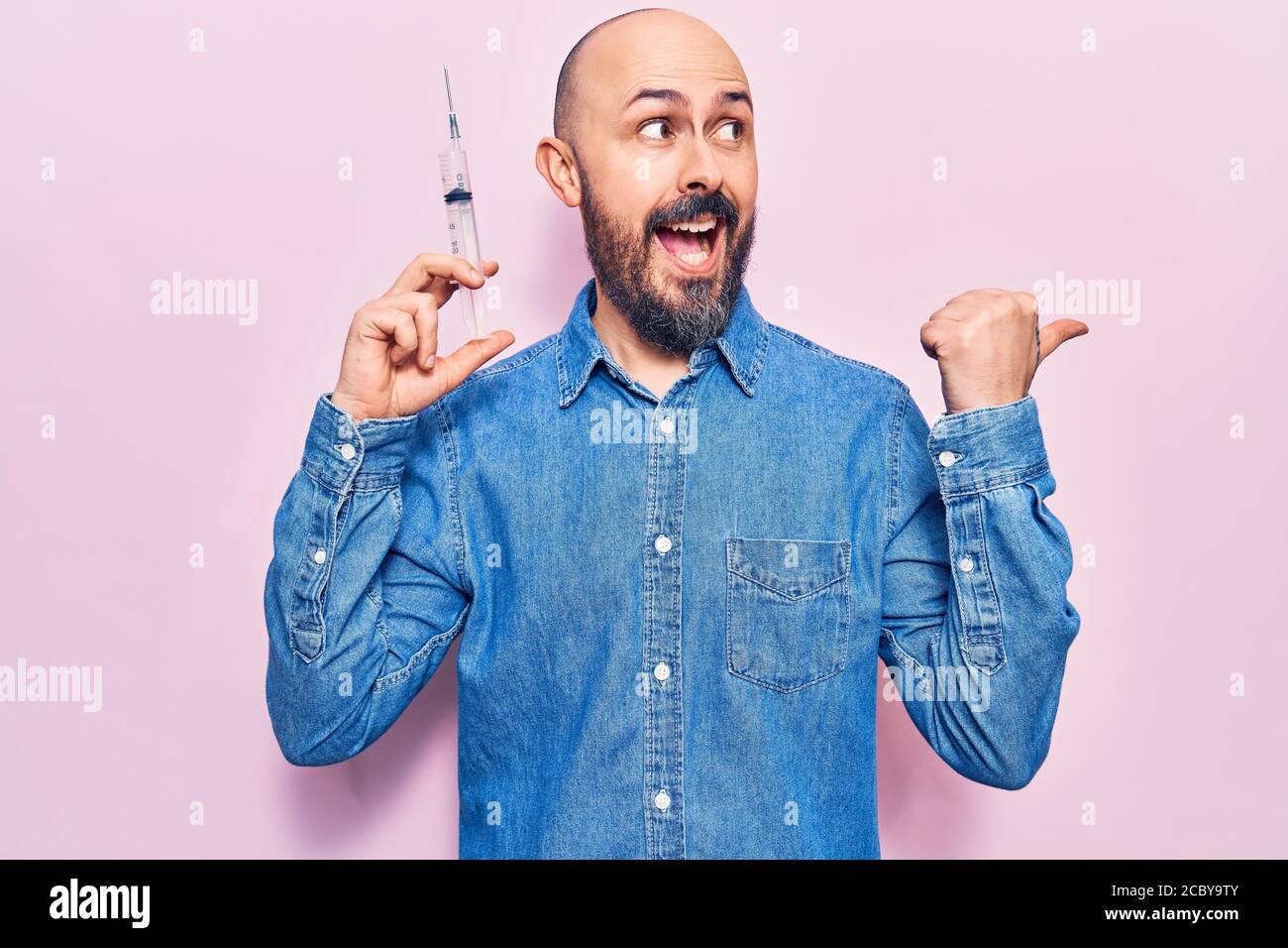 Young handsome man holding syringe pointing thumb up to the side ...