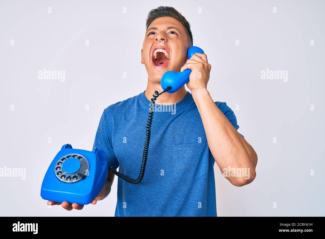 Young hispanic boy holding vintage telephone angry and mad screaming ...