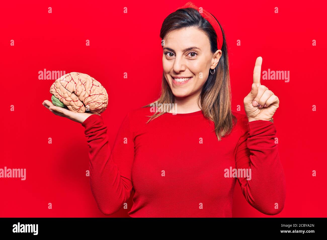 Young beautiful woman holding brain smiling with an idea or question ...