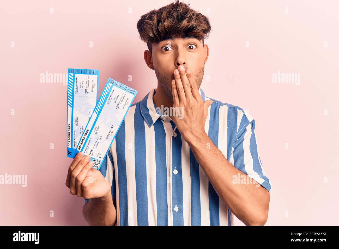 Young hispanic man holding boarding pass covering mouth with hand ...