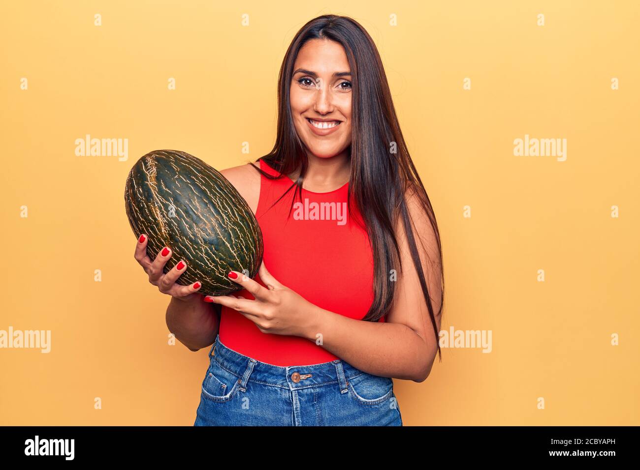 Young beautiful brunette woman holding melon looking positive and happy ...