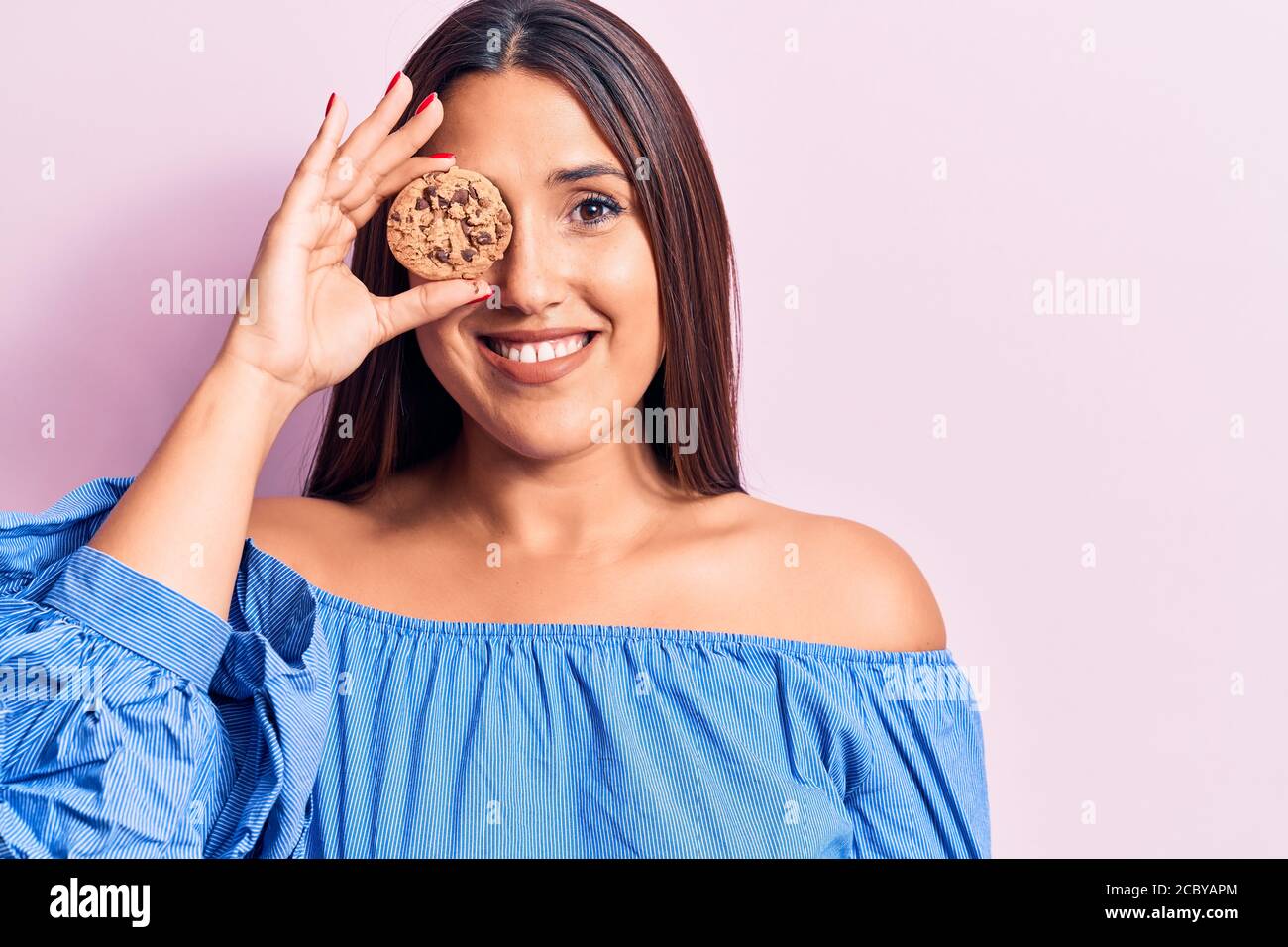 Young beautiful brunette woman holding cookie looking positive and ...