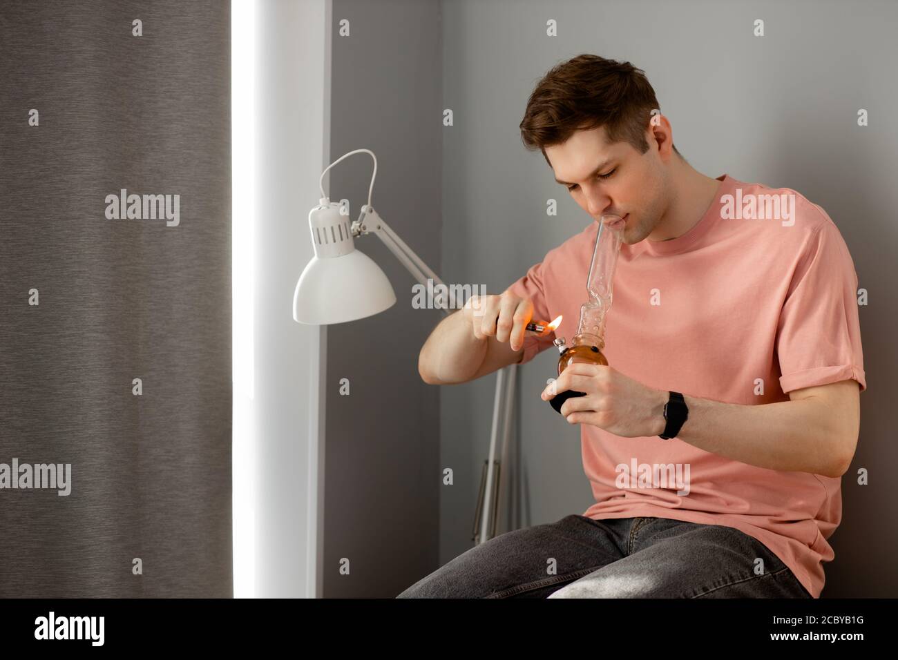 young caucasian man heats bong with marijuana, ganja. young man suffer ...