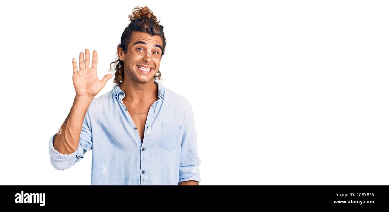 Young hispanic man wearing summer style waiving saying hello happy and ...