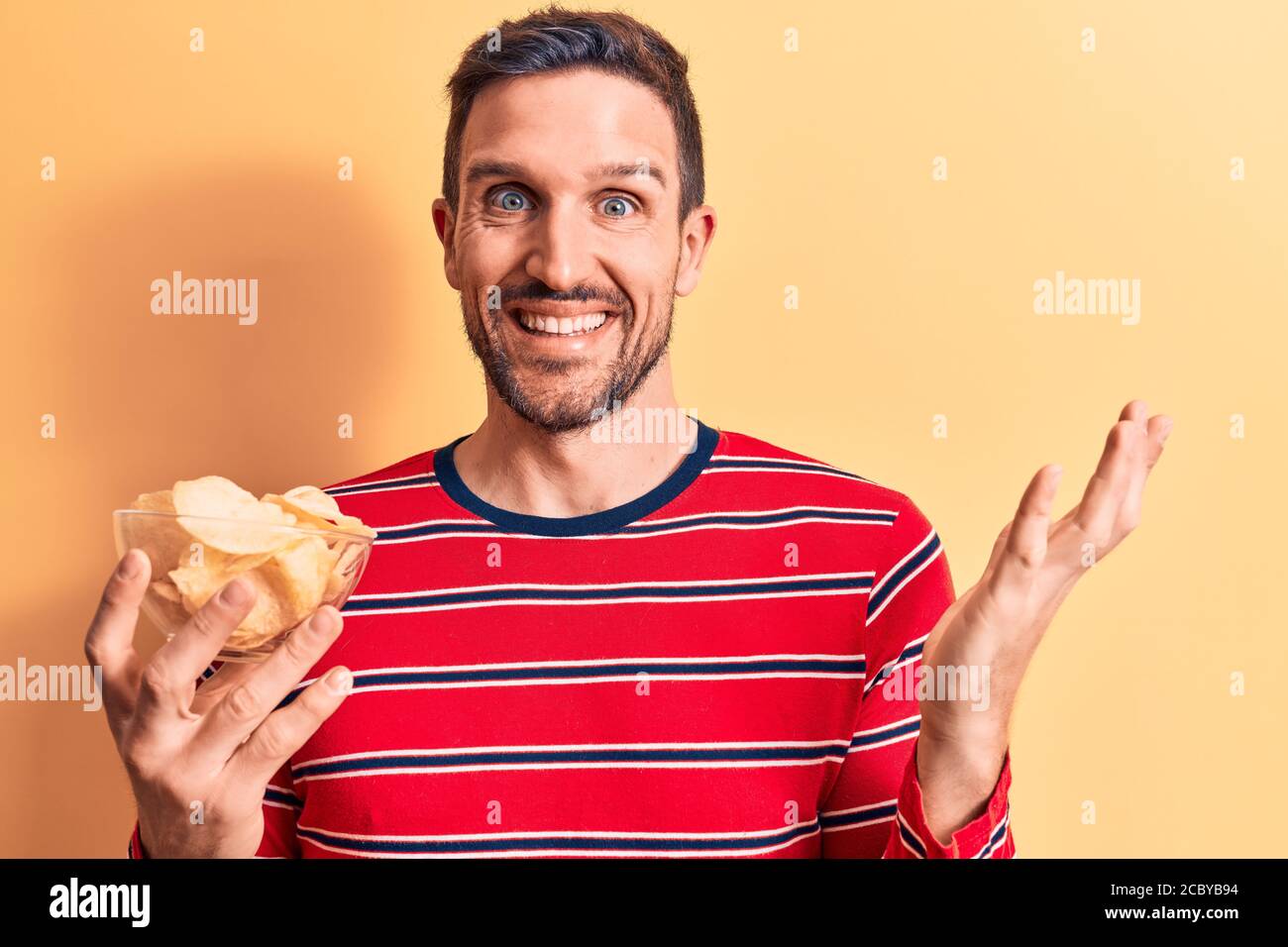 Young handsome man holding bowl of potato chips standing over isolated ...
