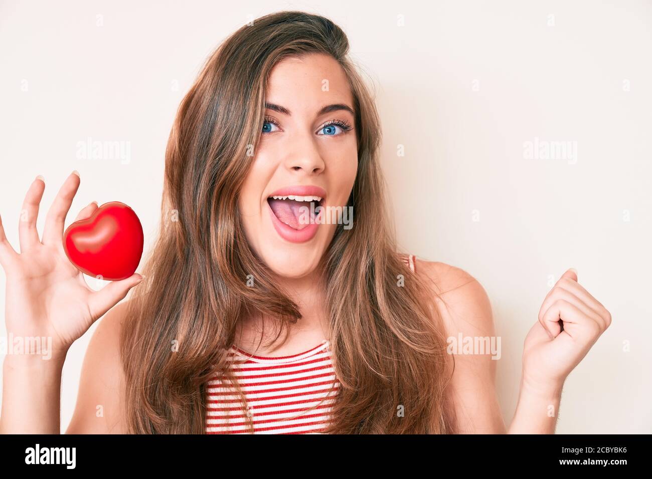 Beautiful young caucasian woman holding heart screaming proud ...