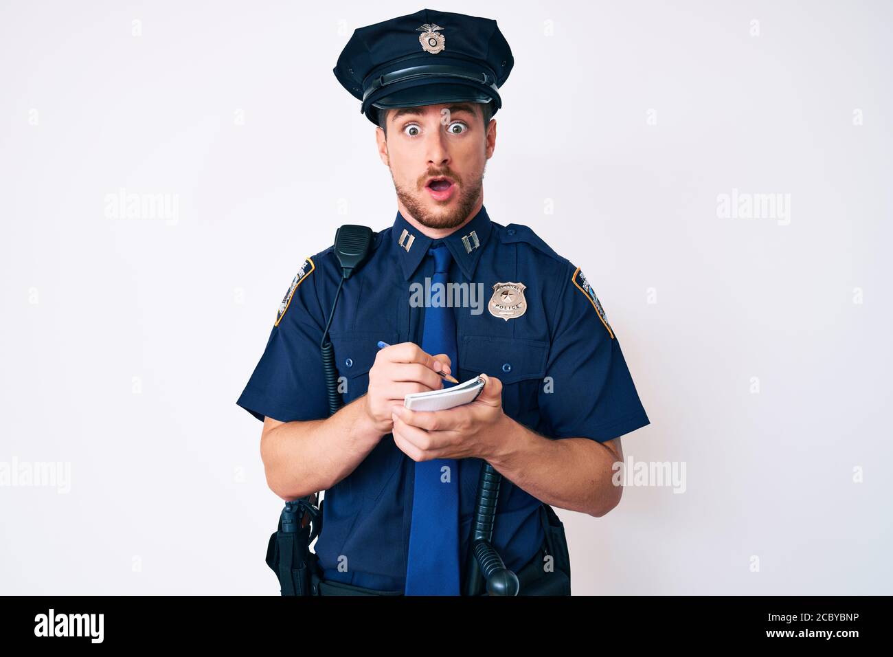 Young caucasian man wearing police uniform writing fine in shock face ...