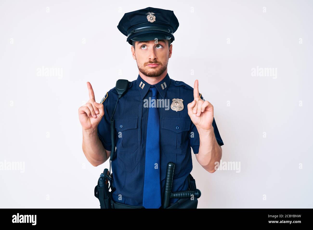 Young caucasian man wearing police uniform pointing up looking sad and ...